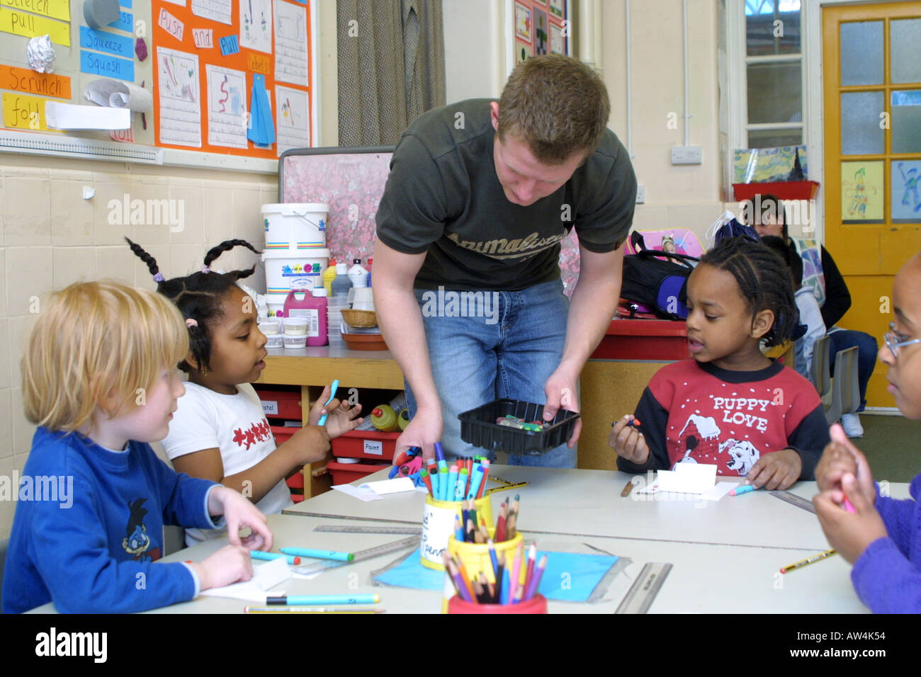 Teacher handing out colour pens to 5 yr old children in a classroom ...