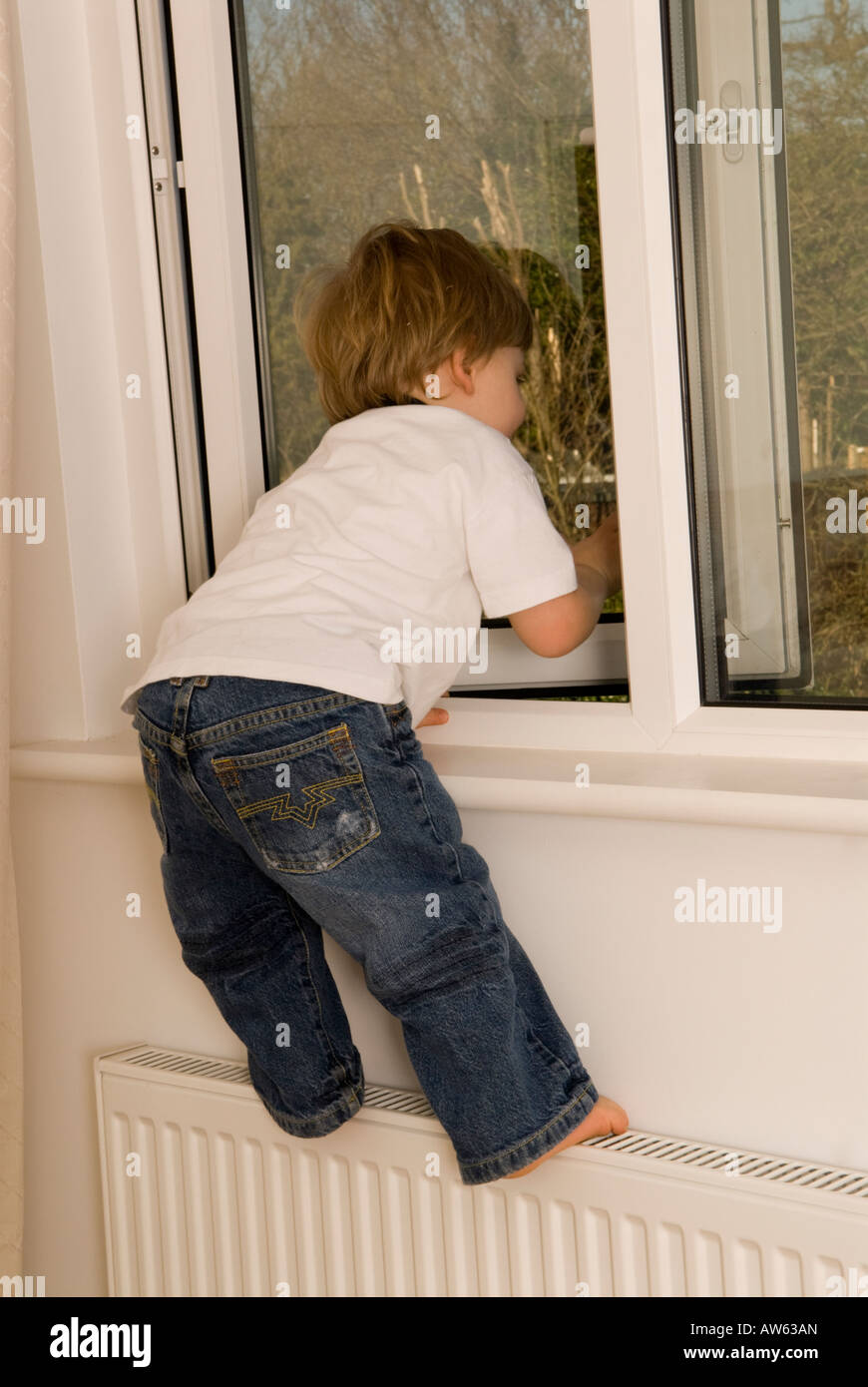 two year old boy in danger climbing up to an open window standing on a ...