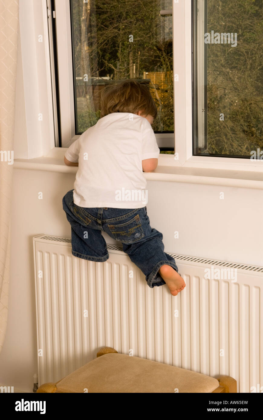 two year old boy in danger climbing up to an open window standing on a ...