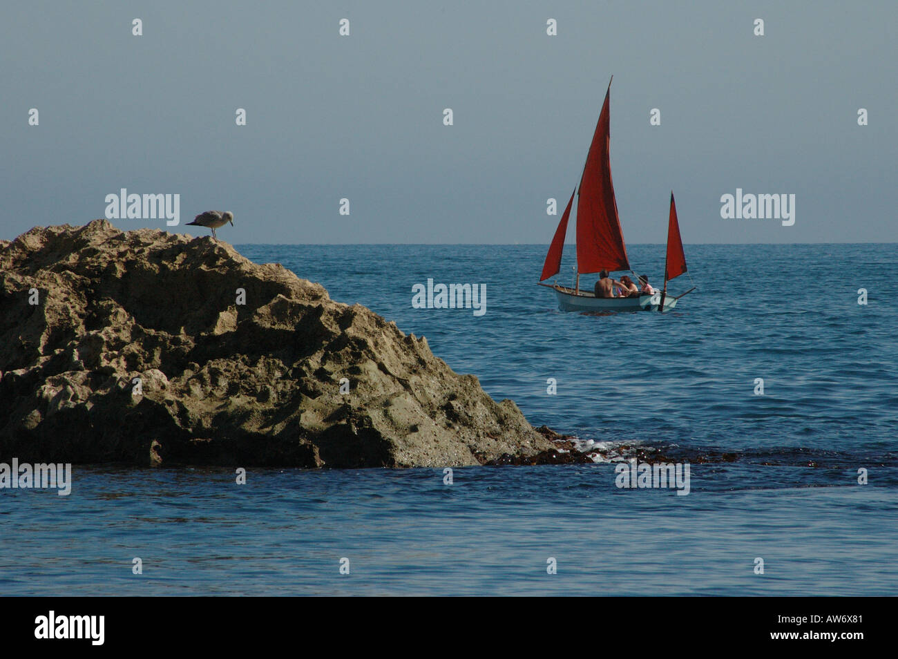 sailing boat with red sails going past a rock in very blue sea Dorset ...
