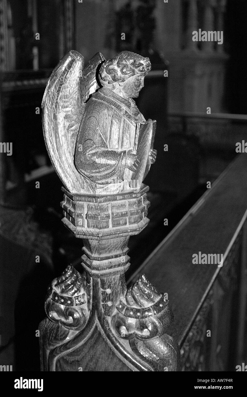 A carved wooden winged figure on the end of a church pew in monochrome ...