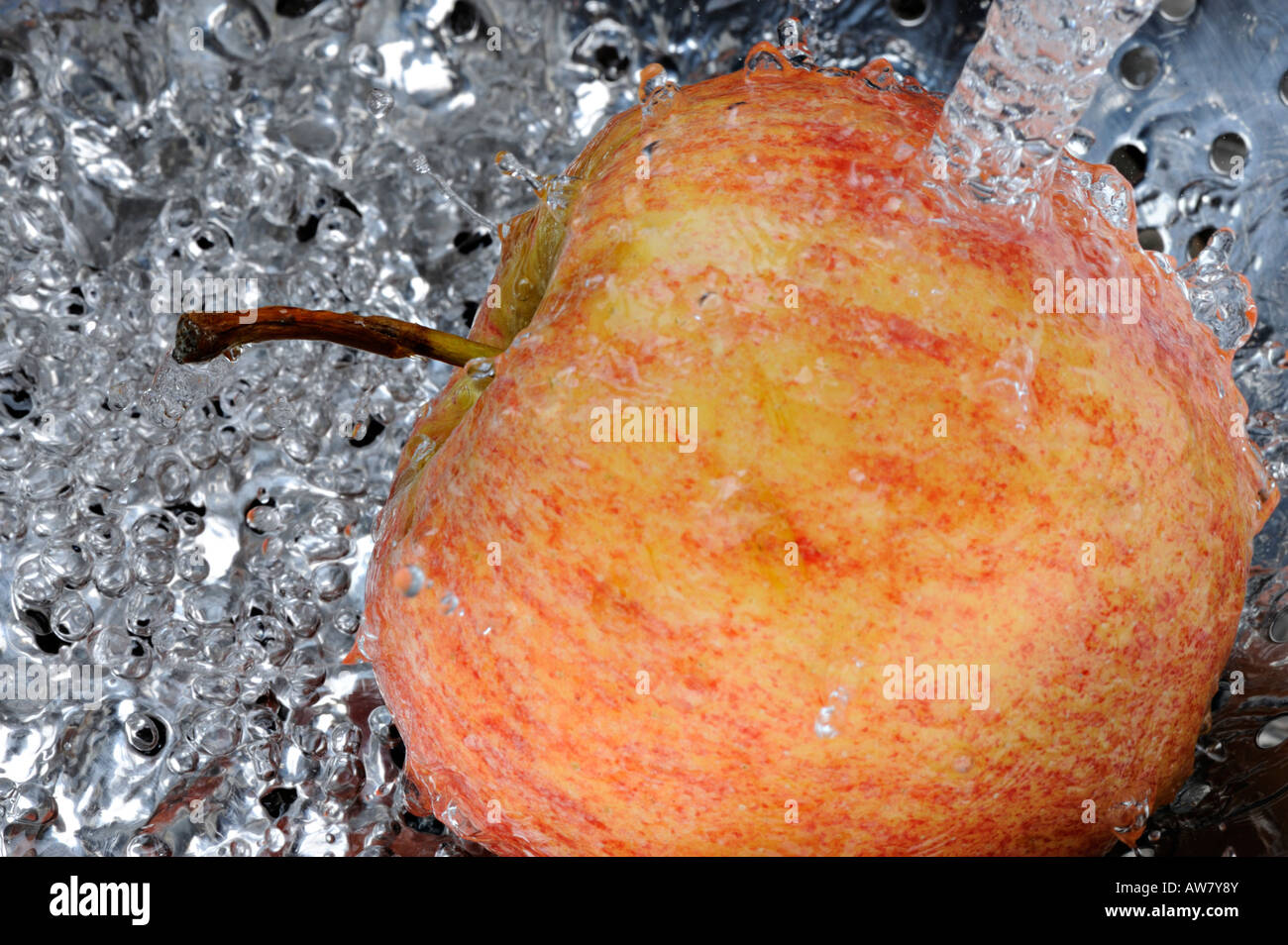 Apple being washed under a jet of water in stainless steel colander ...
