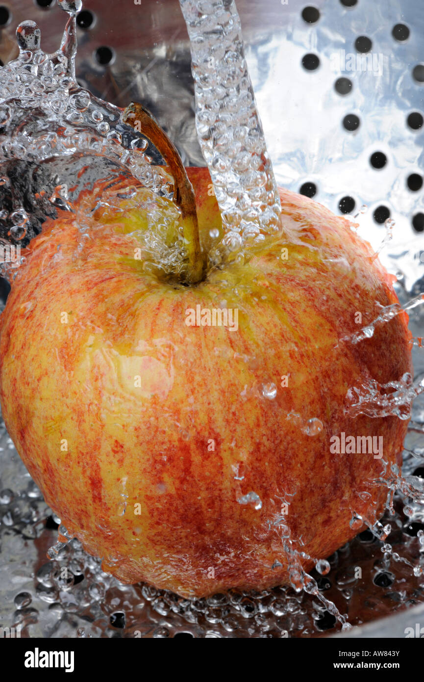 Apple being washed under a jet of water in stainless steel colander ...