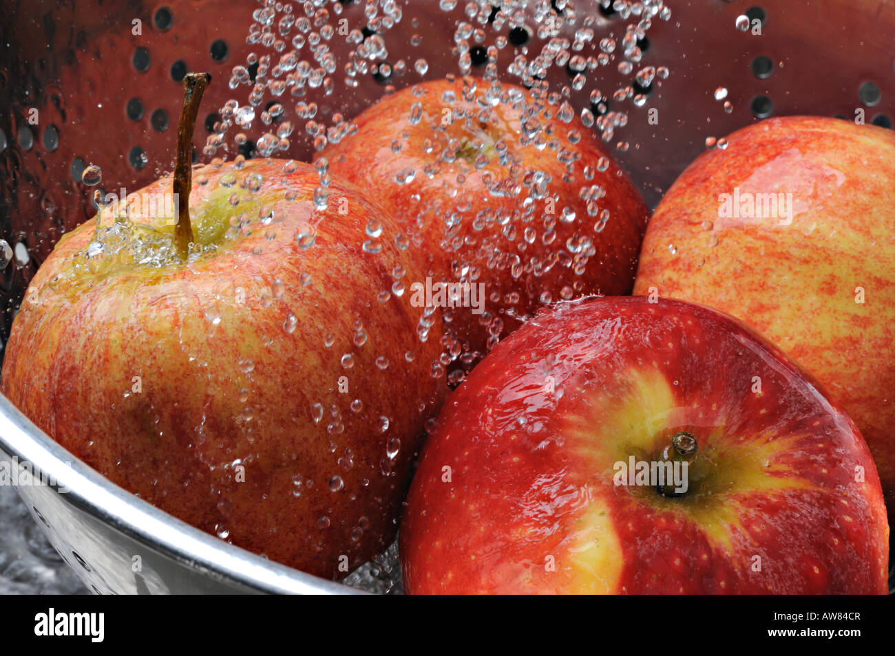 Apples being washed under a jet of water in stainless steel colander ...
