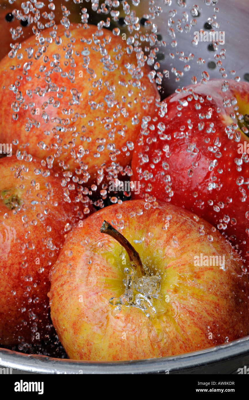 Apples being washed under a jet of water in stainless steel colander ...