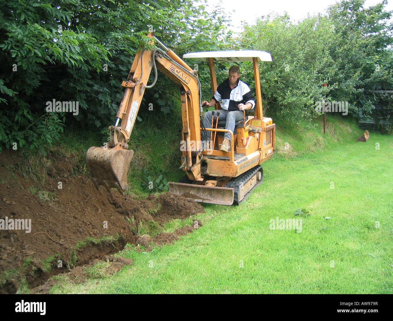 Digger small Caterpilar digging trench in green field for trees Stock ...