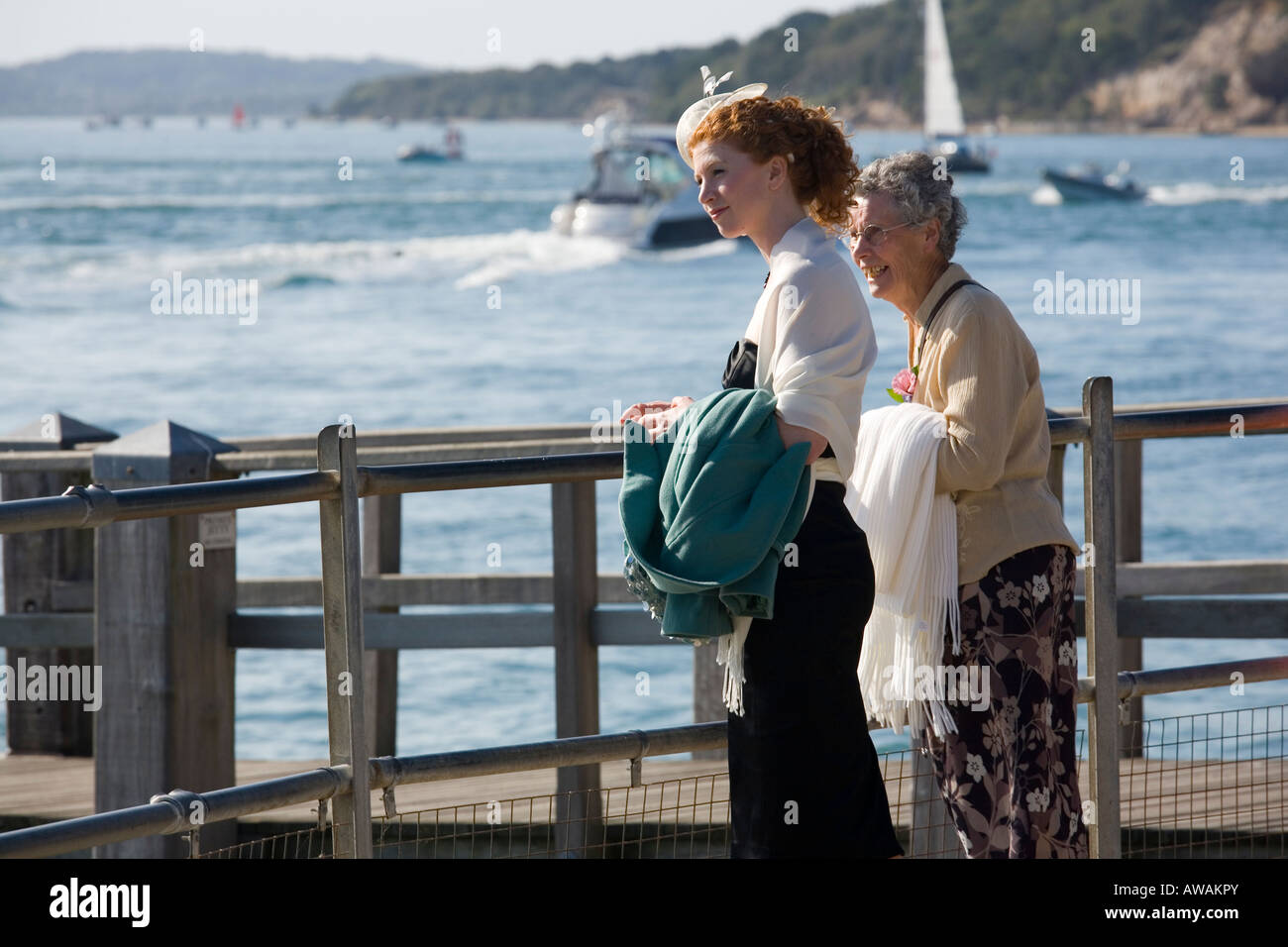 Two ladies dressed for a wedding watch the boats at Poole Harbour ...
