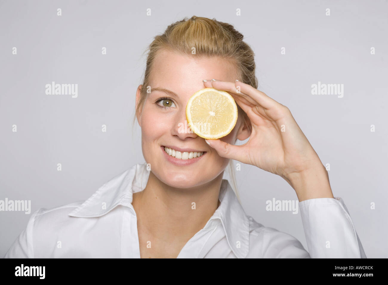 Young woman holding a lemon slice in front of one eye Stock Photo - Alamy