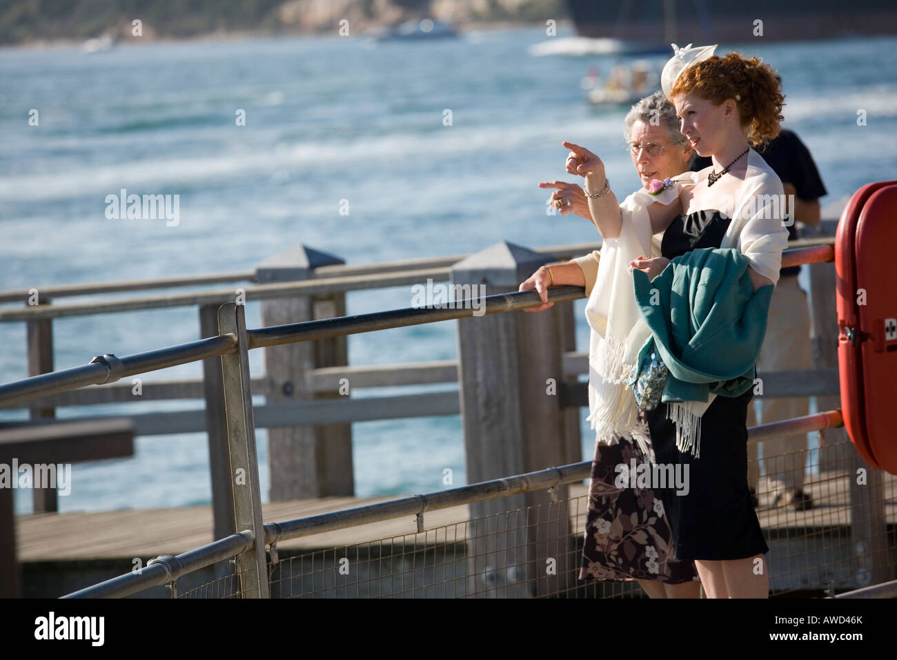 Two ladies dressed for a wedding watch the boats at Poole Harbour ...