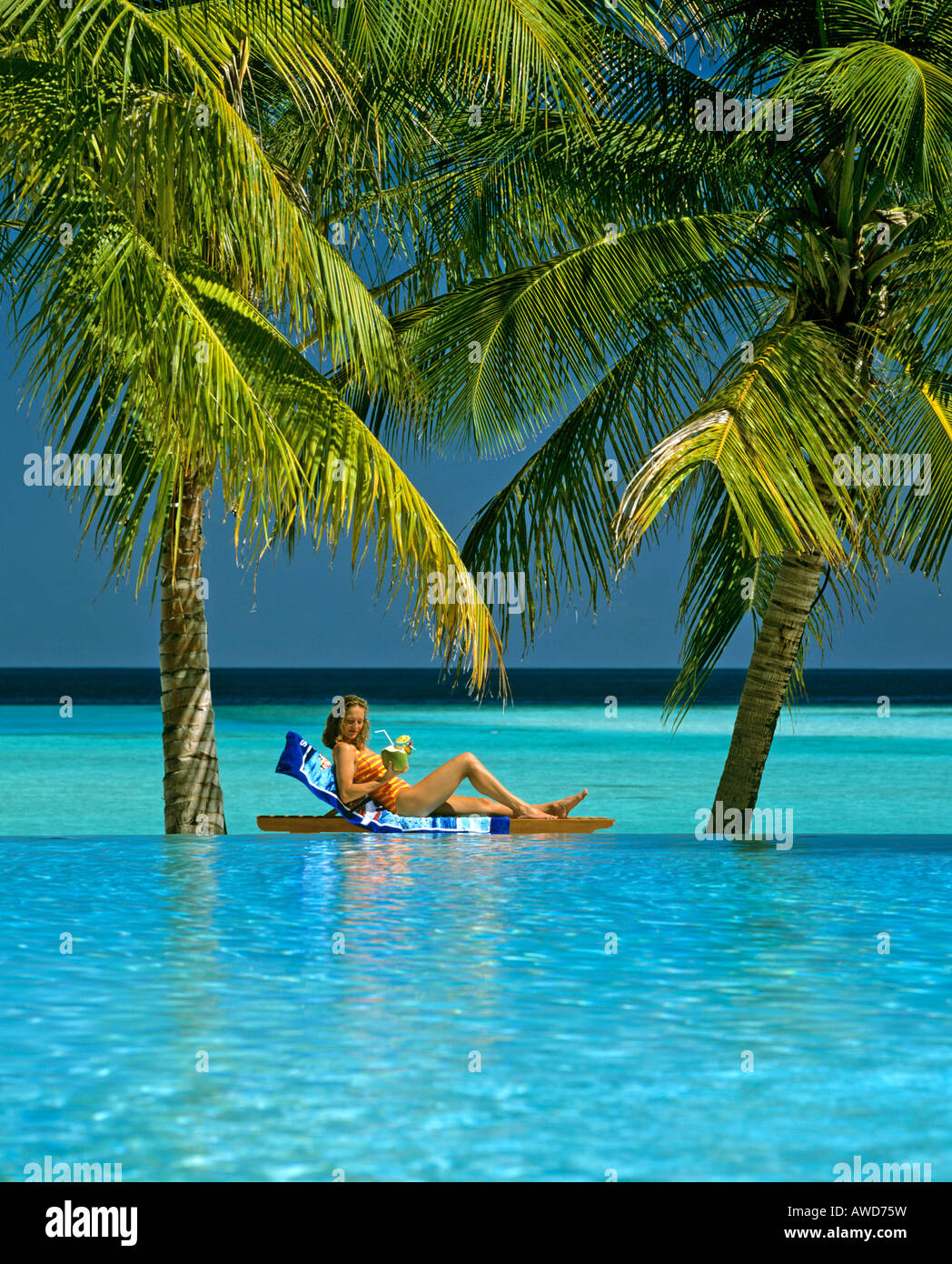 Young woman holding drink, laying on deck chair, swimming pool, ocean ...