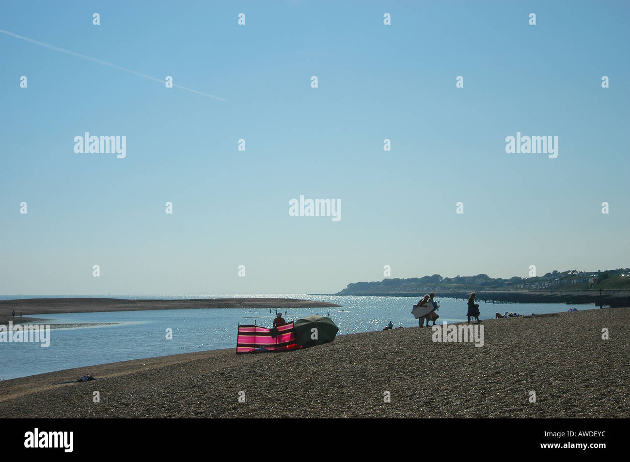 Bright pink wind shield on a shingle beach with bathers on a fine day ...