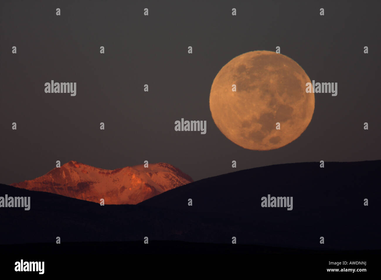 Telephoto image of the full moon setting over a volcano lit by the ...