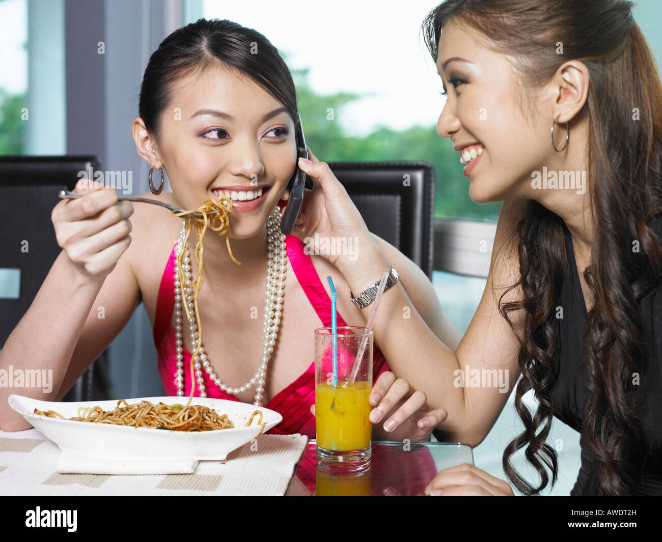 two young women using cell phone while eating at restaurant Stock Photo ...