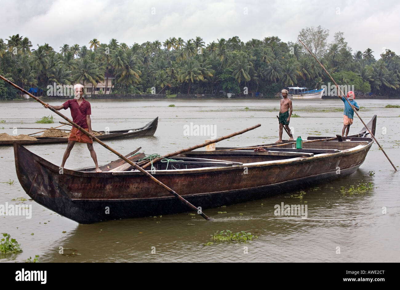 Rural men paddling wooden canoes in Kerala Blackwaters against a ...