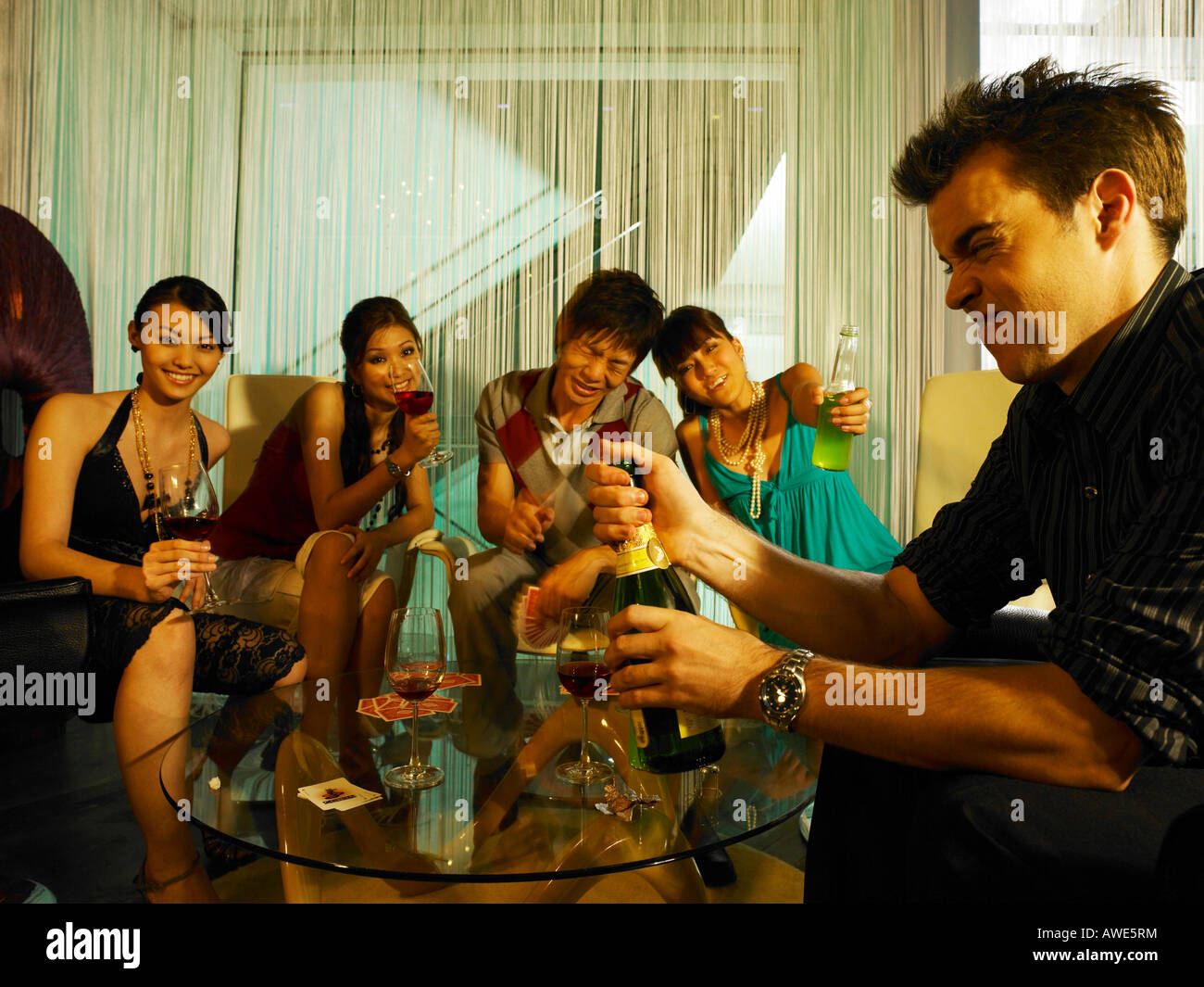 man trying hard to open champagne, friends laughing at him Stock Photo ...