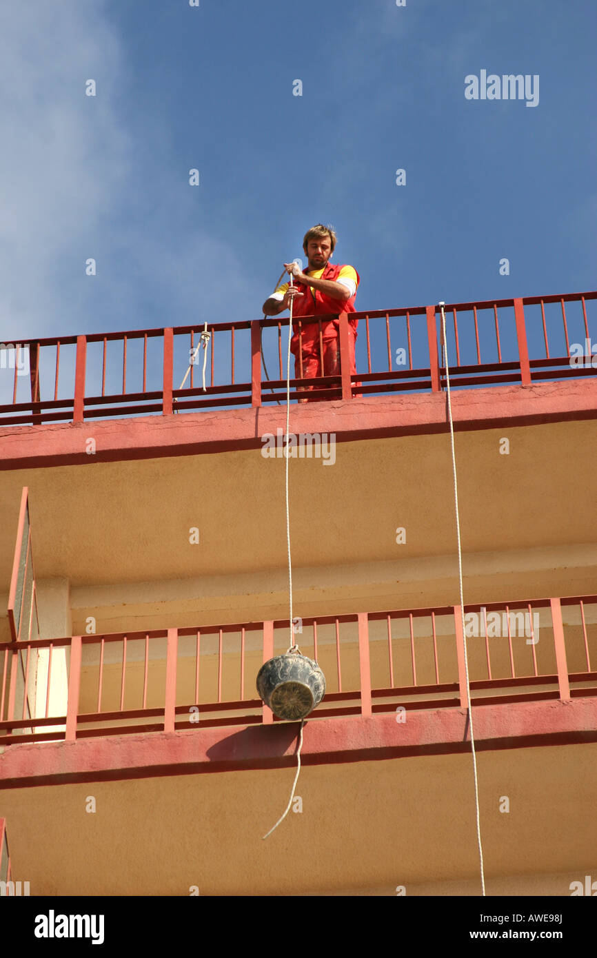 Workman lifting bucket of material with rope on building site in ...