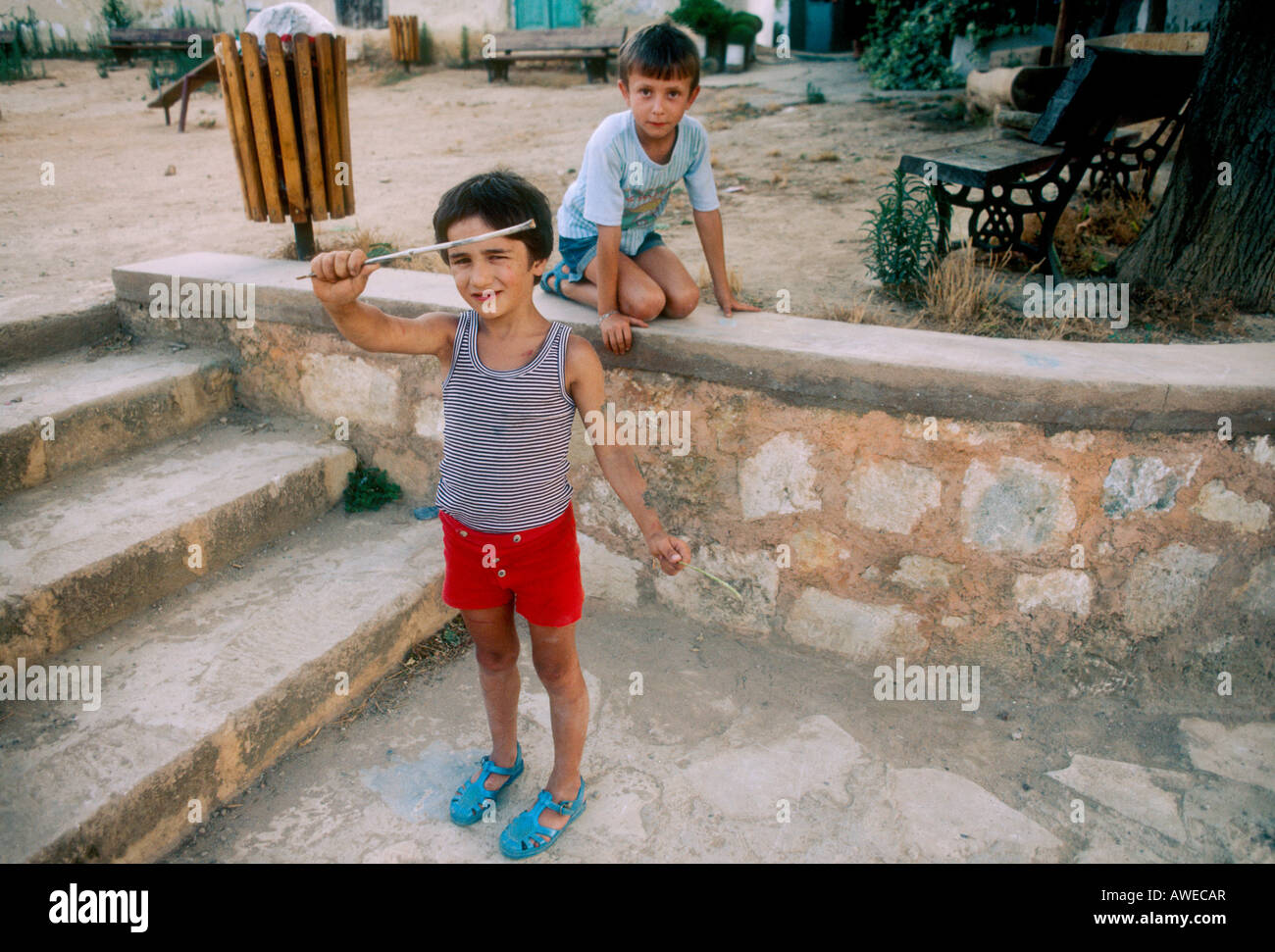 Two young boys playing one boy holding stick up in small park in the ...