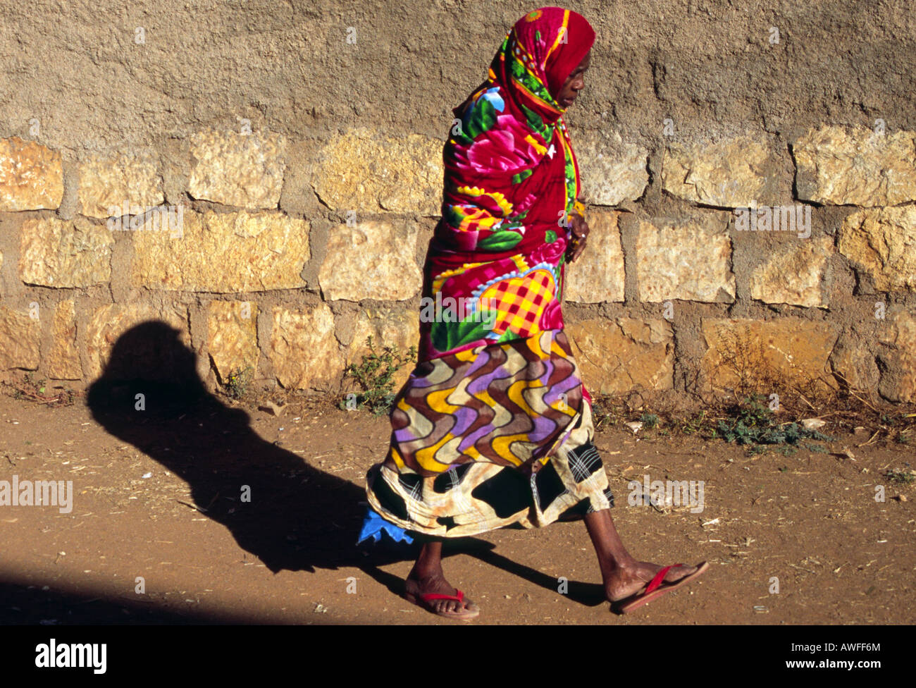 A woman in bright coloured traditional clothes walks past a wall in ...