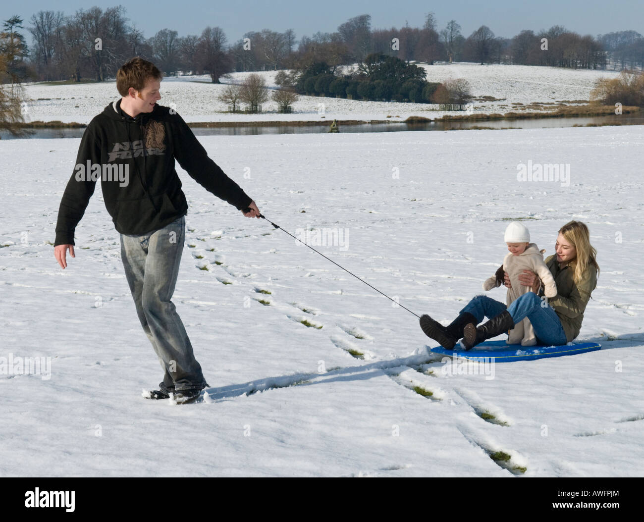 father pulling wife and one year old baby on sledge over snow Stock ...
