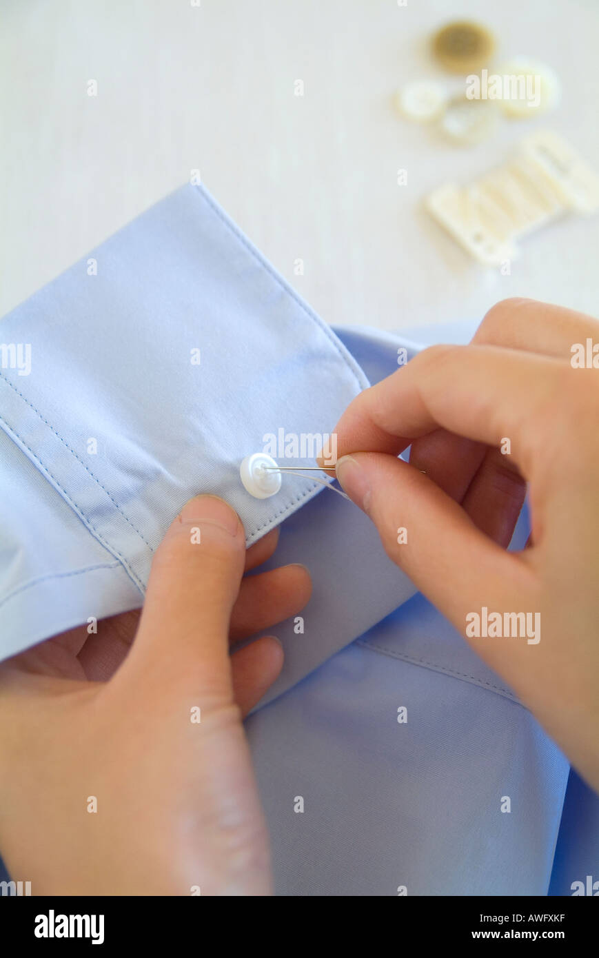 A woman sewing button on shirt Stock Photo - Alamy