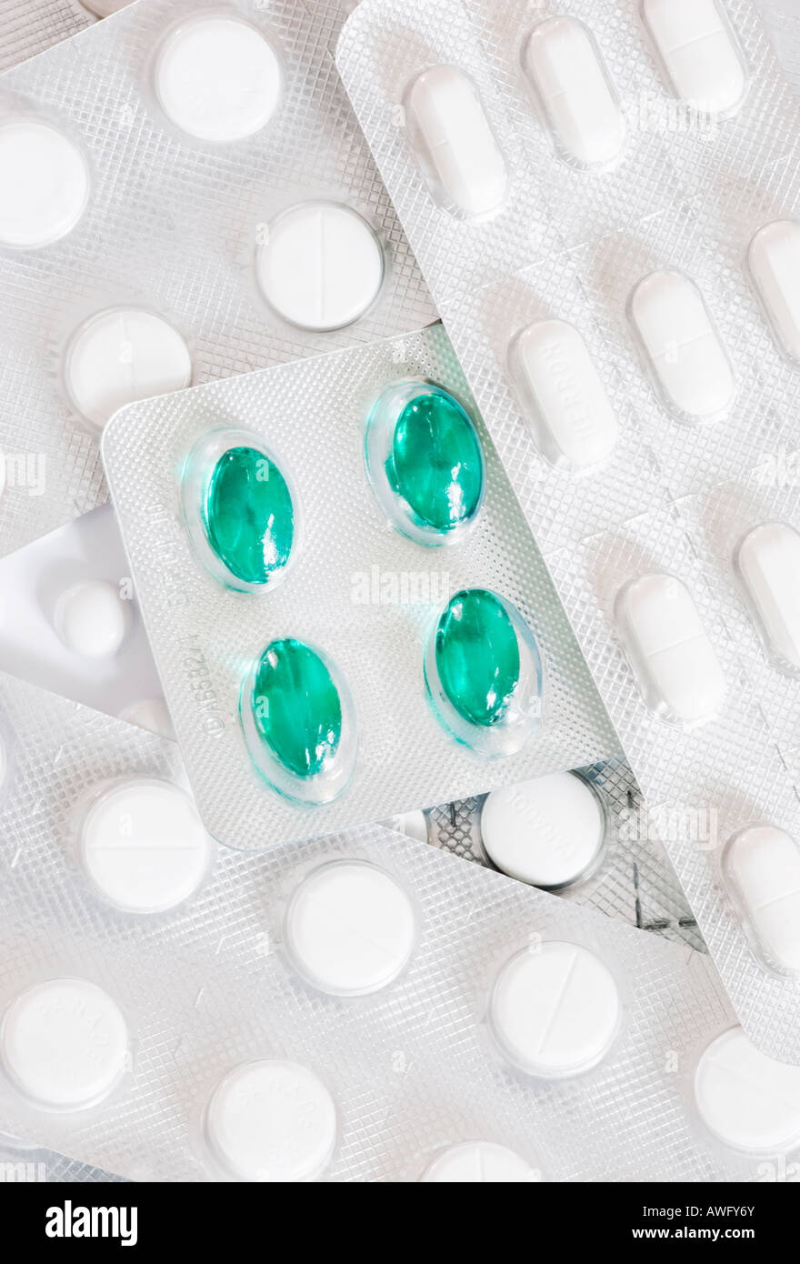 Green tablets against a background of white pills in blister packs ...