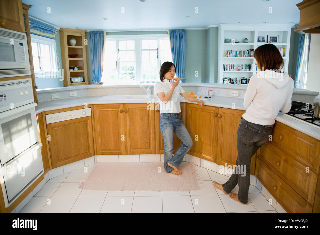 Two young women talking in kitchen Stock Photo - Alamy