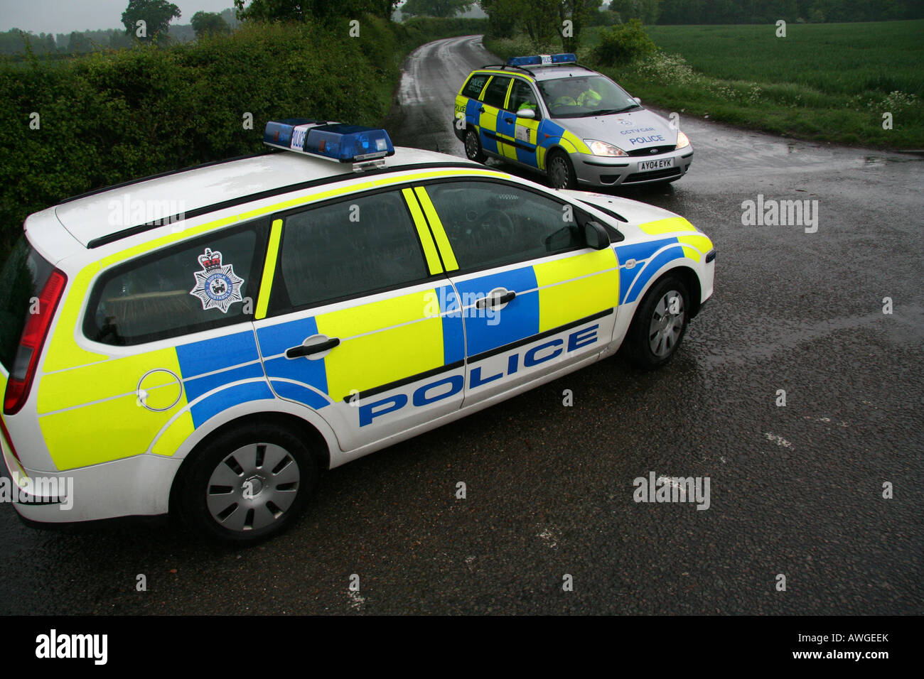 Two police cars waiting at the junction of two wet country roads in ...