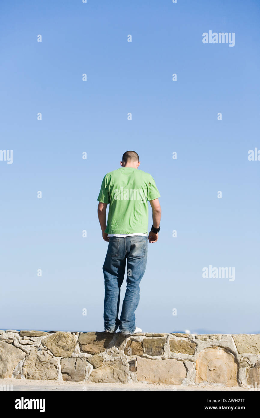 Young man standing alone on a wall with blue sky as background Stock ...