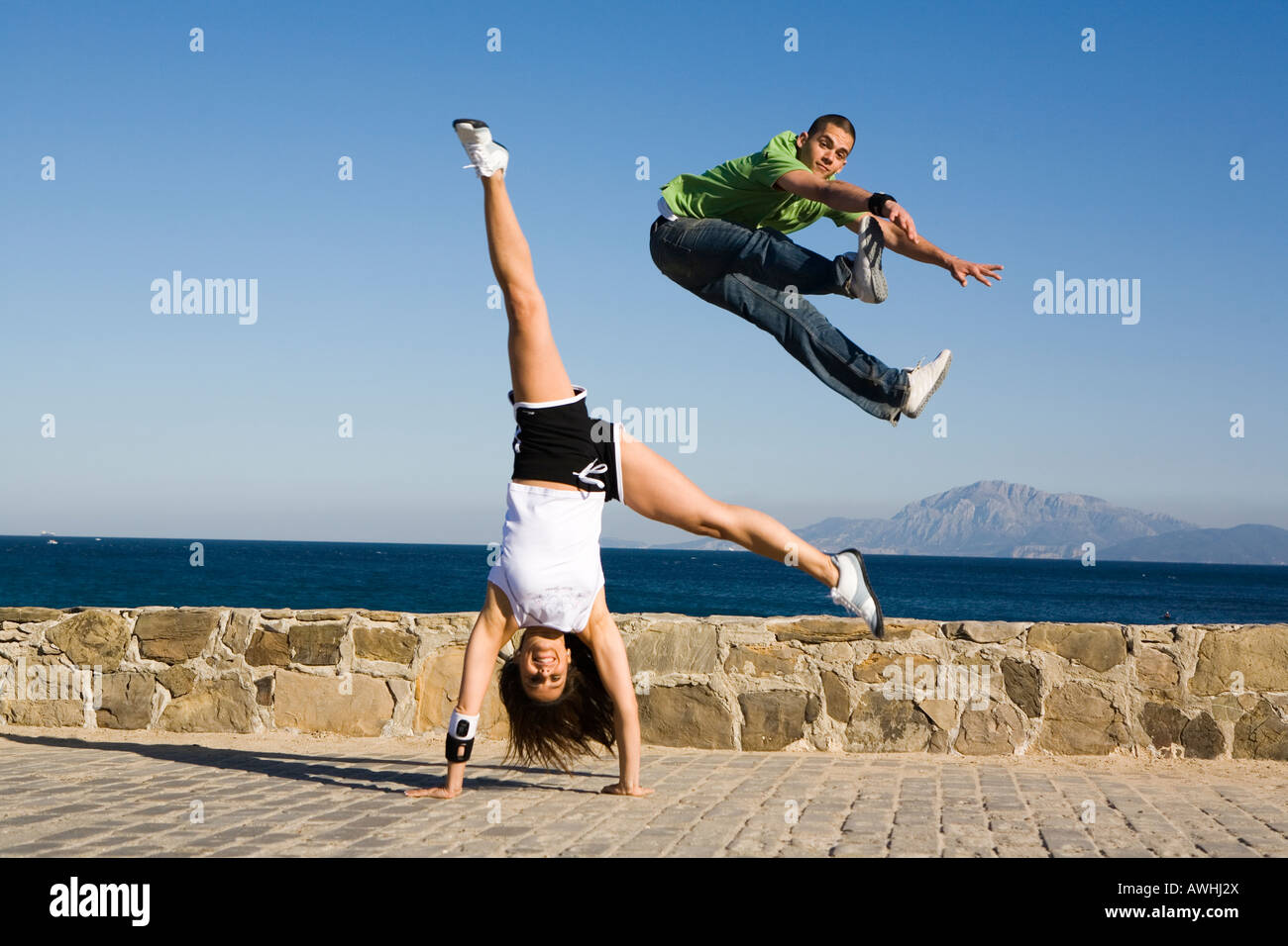 Young man jumping over woman doing handstand Stock Photo - Alamy