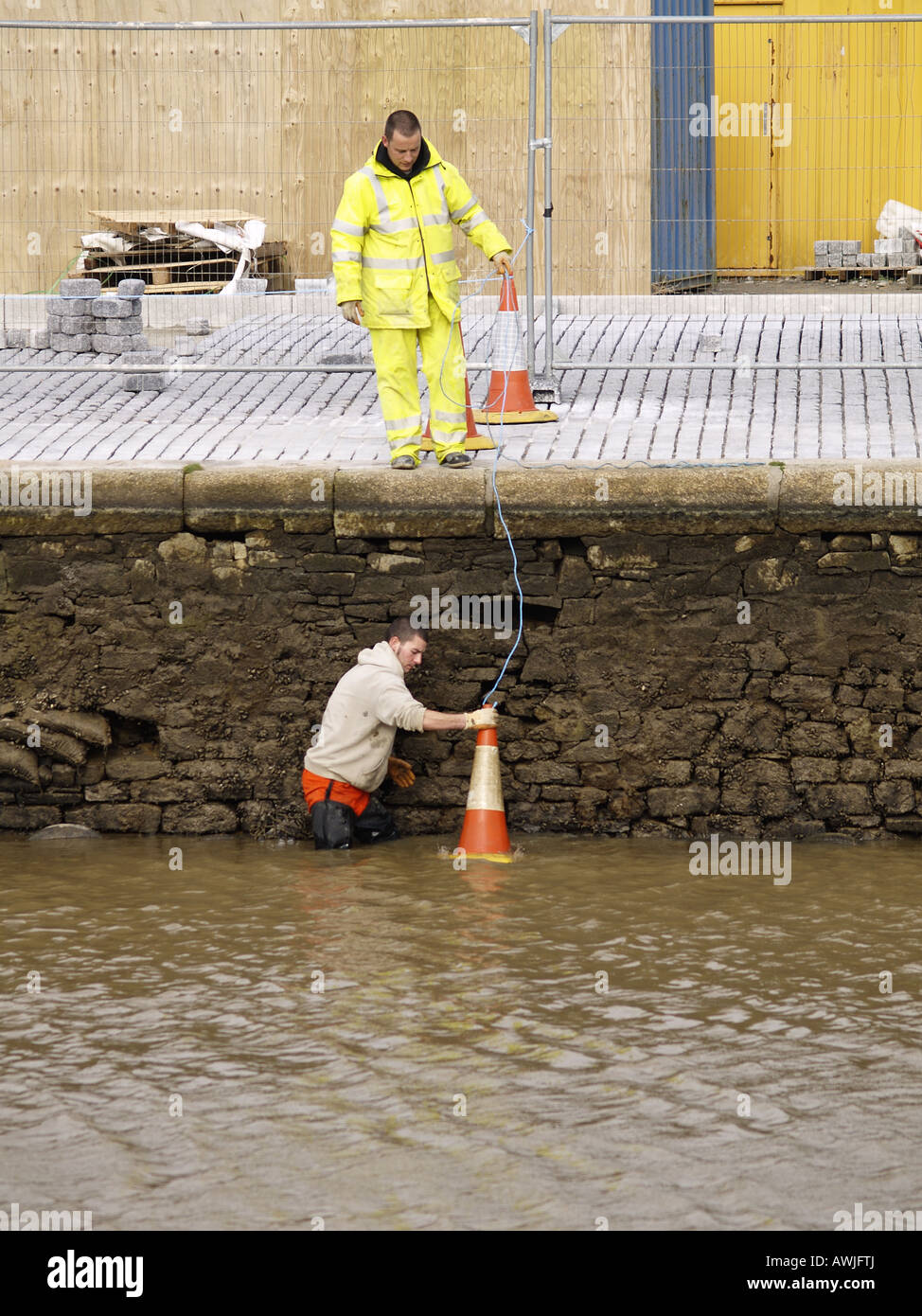 Workman rescuing traffic cones from canal after they were blown in by ...