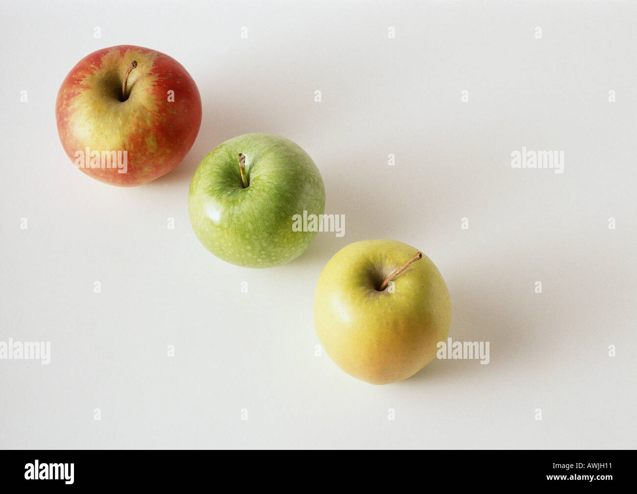 Three apples, red, green, yellow, in diagonal line, against white ...