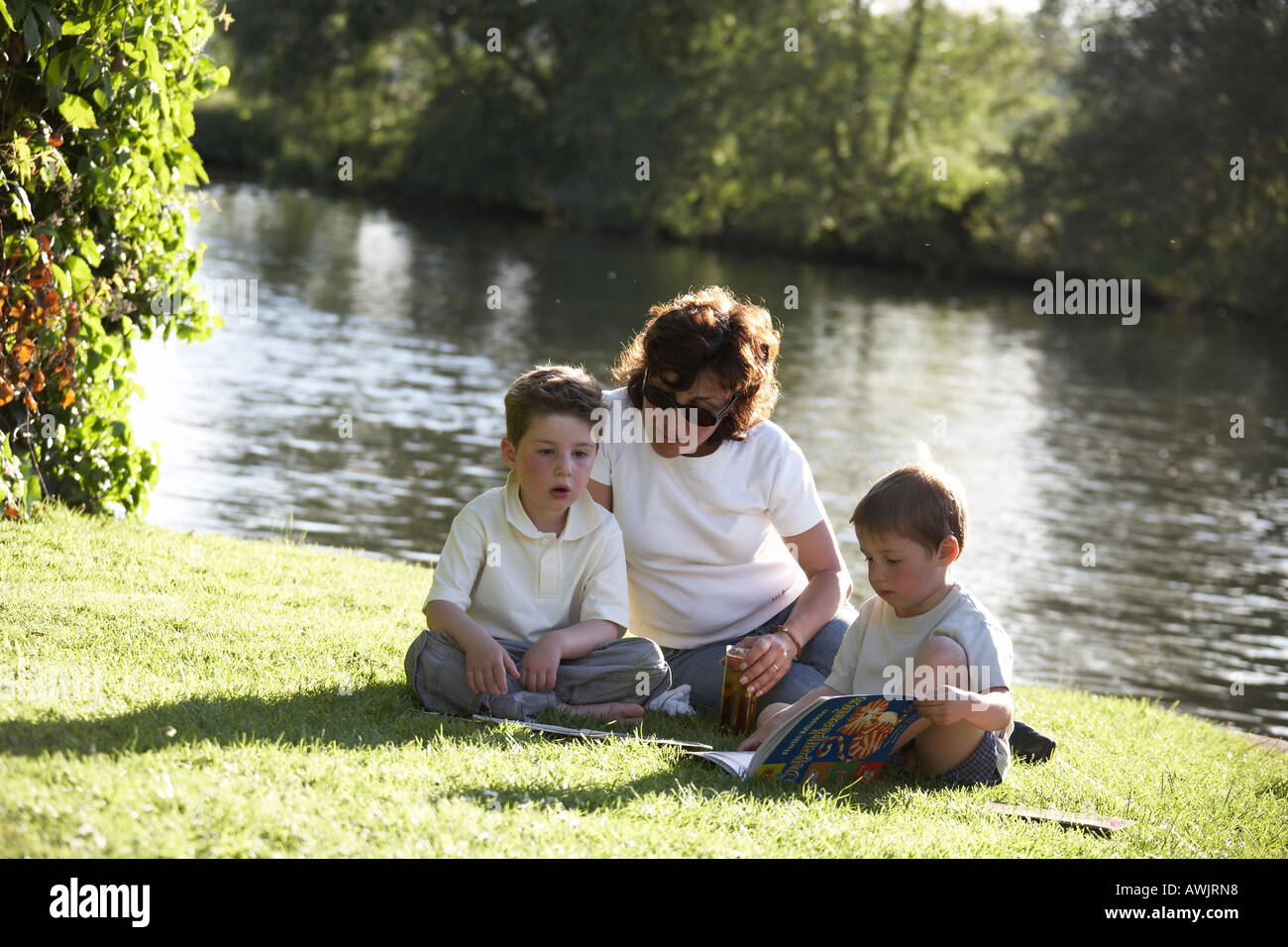Mother and boy children reading on grass beside river near Shiplake on ...