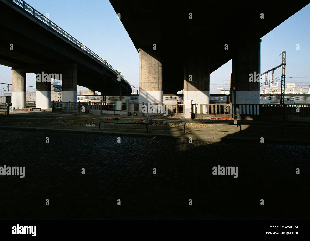 Road underneath bridges, train moving in background Stock Photo - Alamy