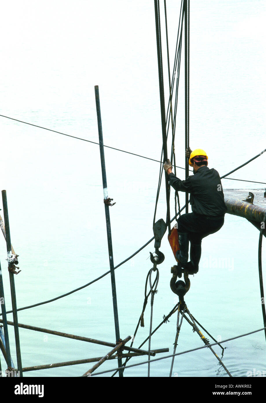 Man with hard hat holding on to cables above water Stock Photo - Alamy