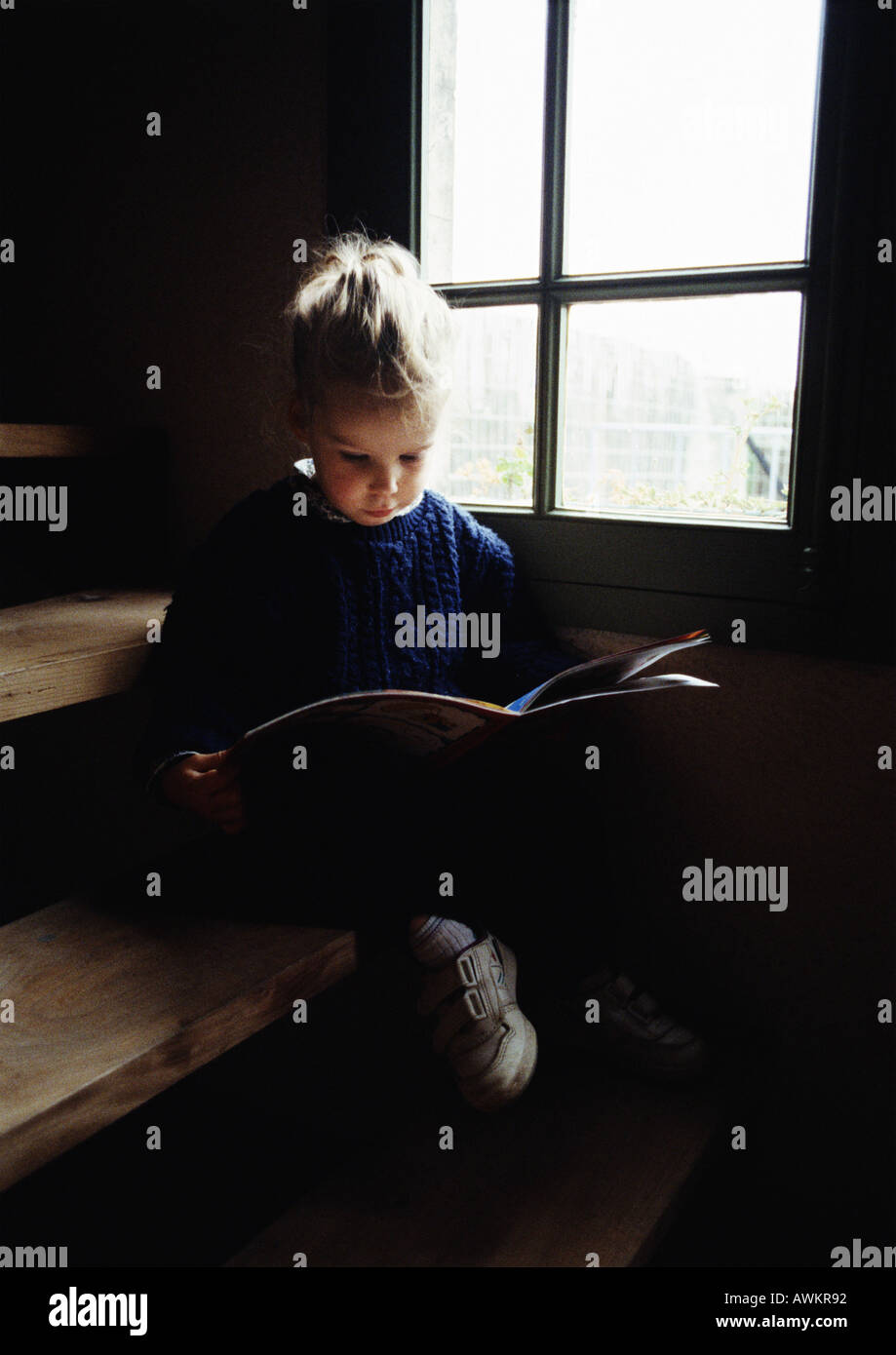 Little boy sitting near window, reading Stock Photo - Alamy