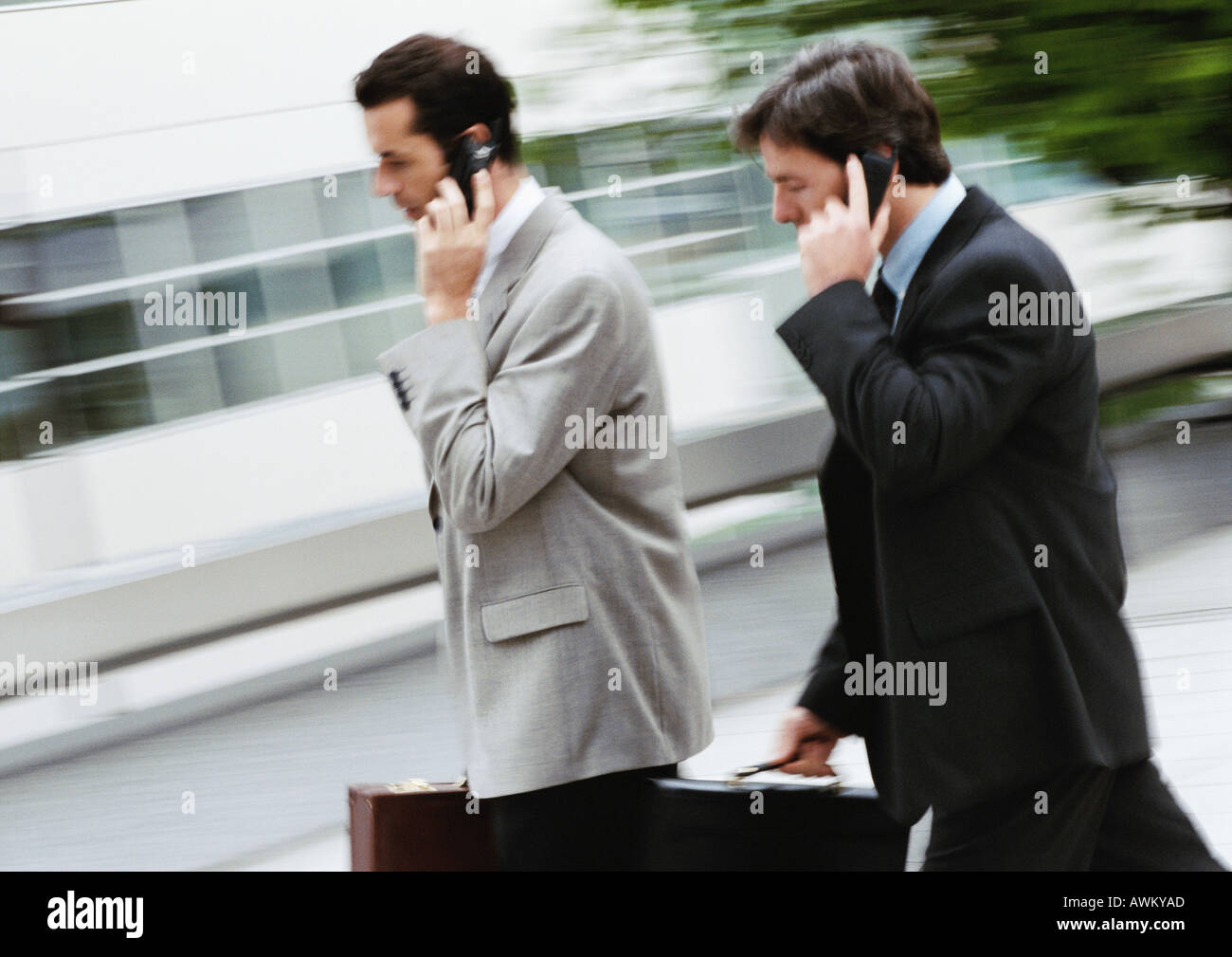 Two businessmen holding briefcase and cell phone, walking outside Stock Photo - Alamy