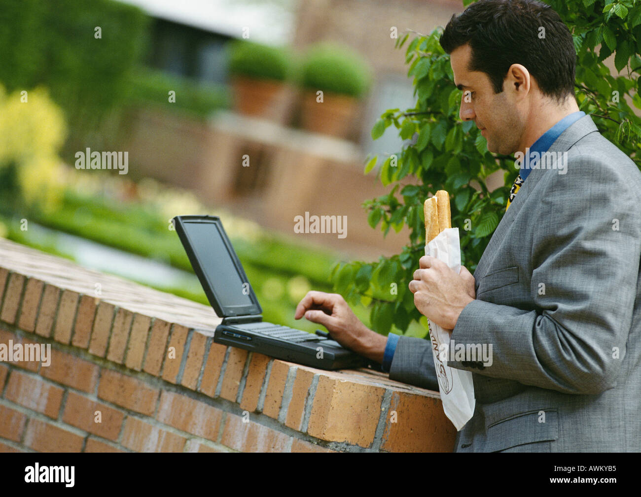 Businessman using laptop computer while eating sandwich outside Stock ...