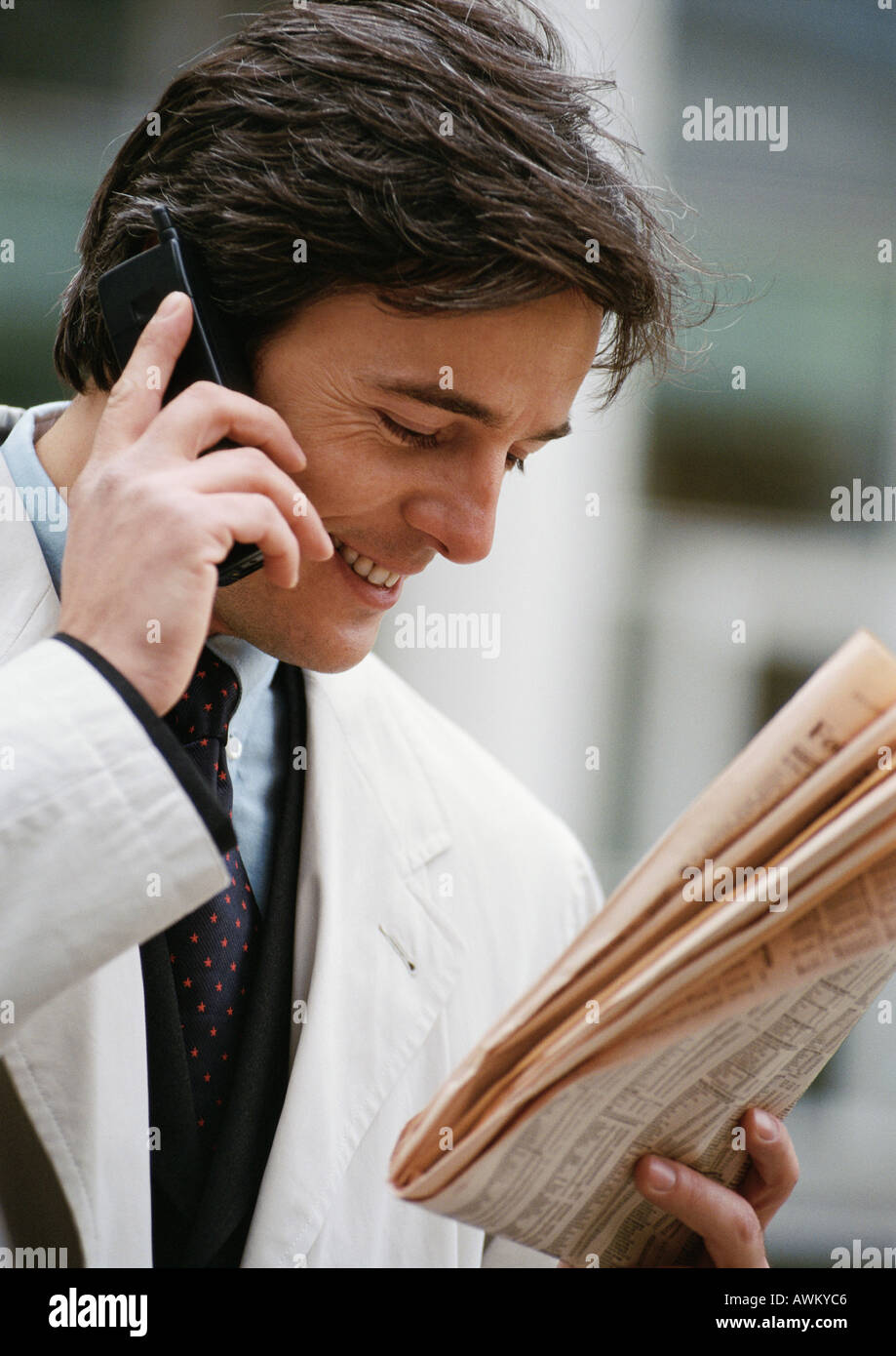 Businessman using cell phone while looking at newspaper Stock Photo - Alamy
