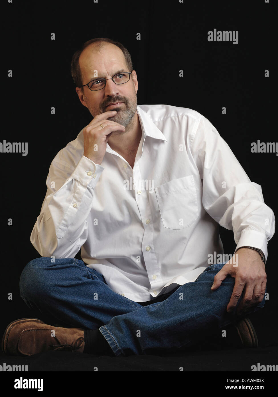 Thoughtful middle-aged man sitting cross-legged Stock Photo - Alamy