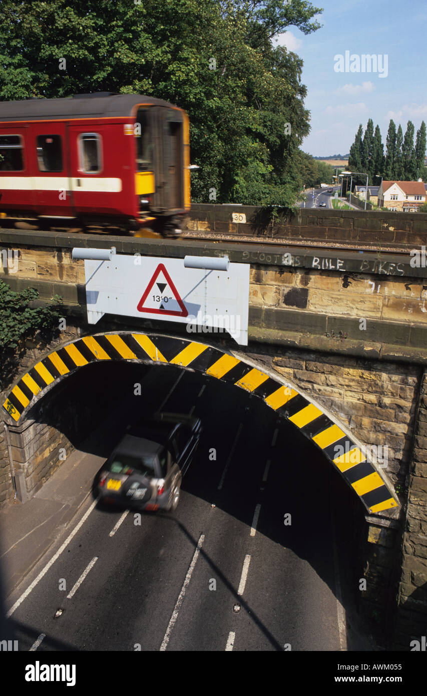 vehicle passing under low railway bridge with train passing over the ...