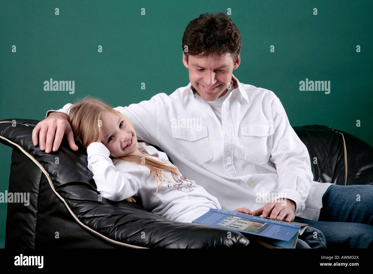 Father And Daughter Sitting On The Couch The Daughter With A Book In