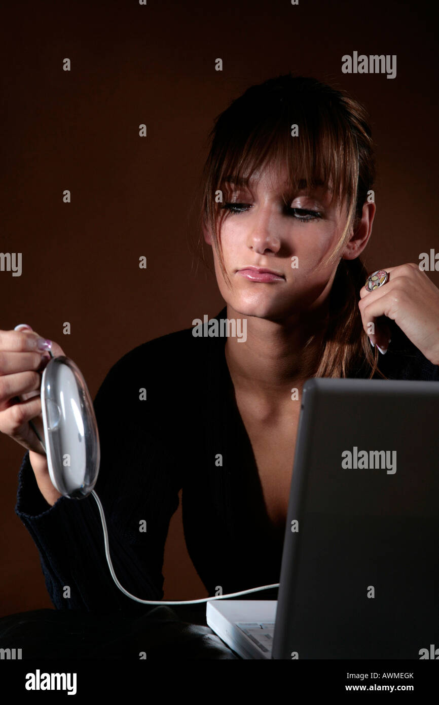 Young woman sitting in front of a laptop holding the mouse, looking ...