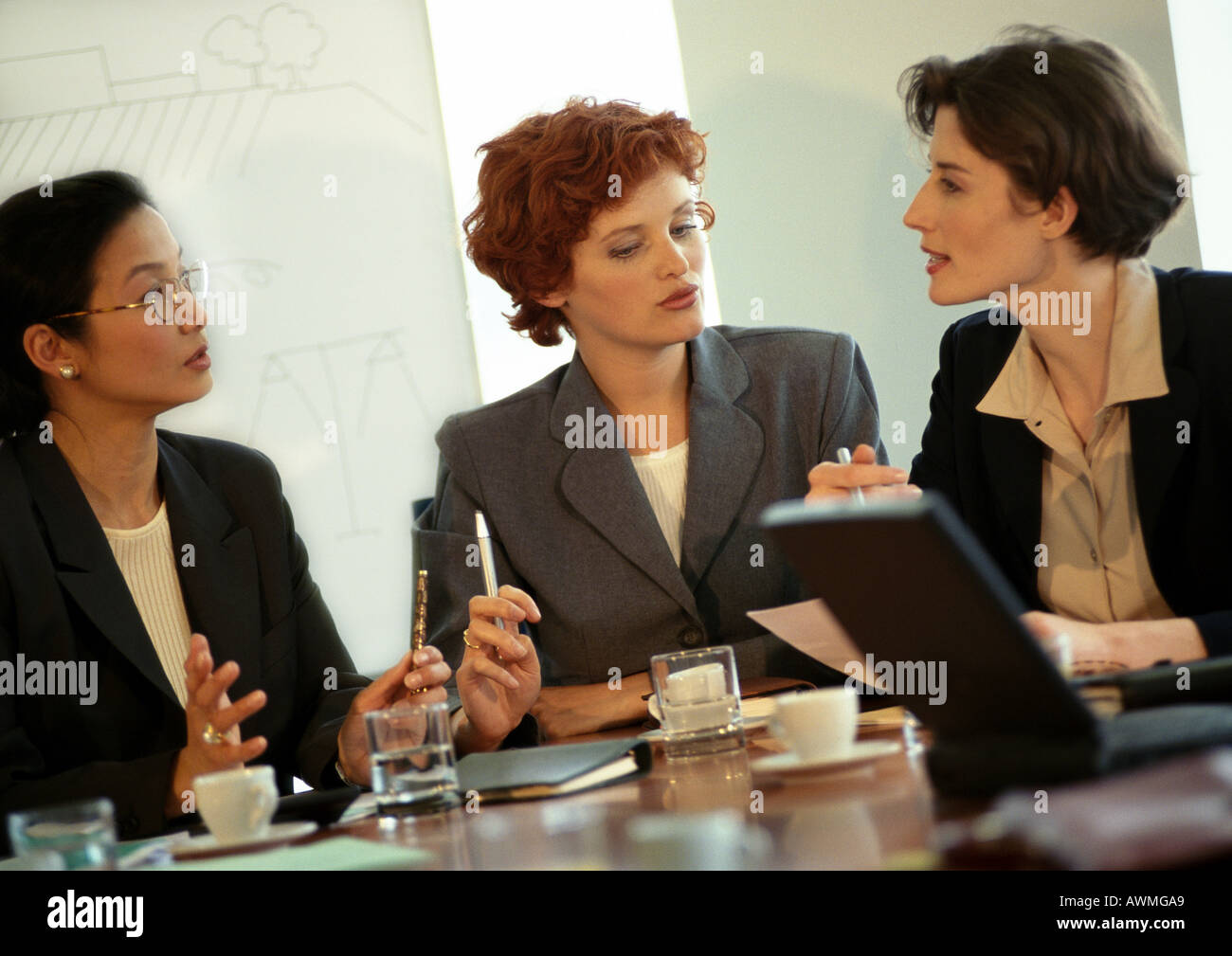Three businesswomen sitting at conference table, talking Stock Photo ...