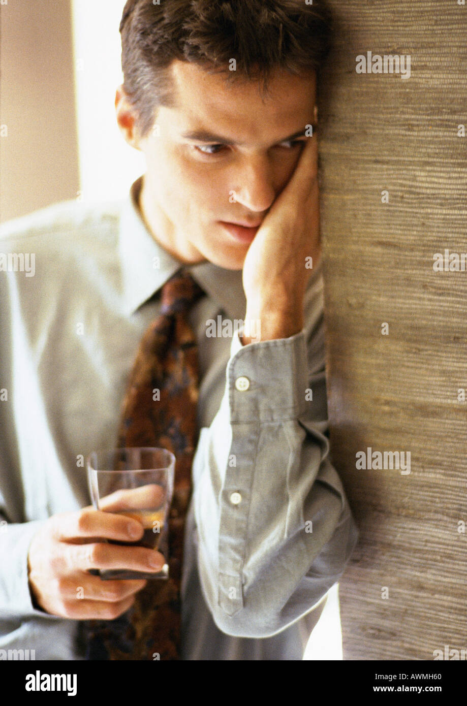 Man with hand against face leaning against wall and holding glass ...