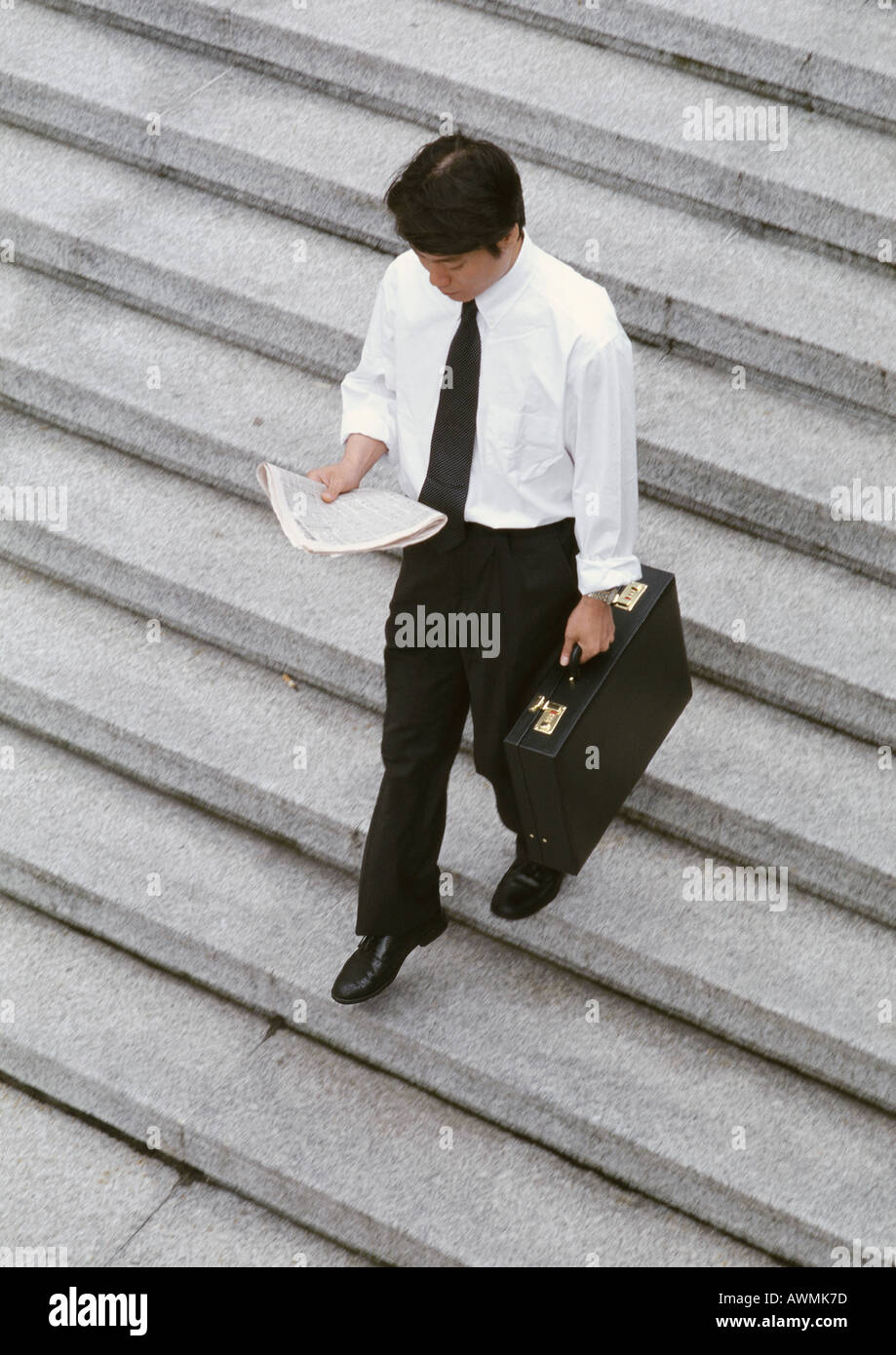 Businessman reading newspaper while walking down steps, high angle view ...