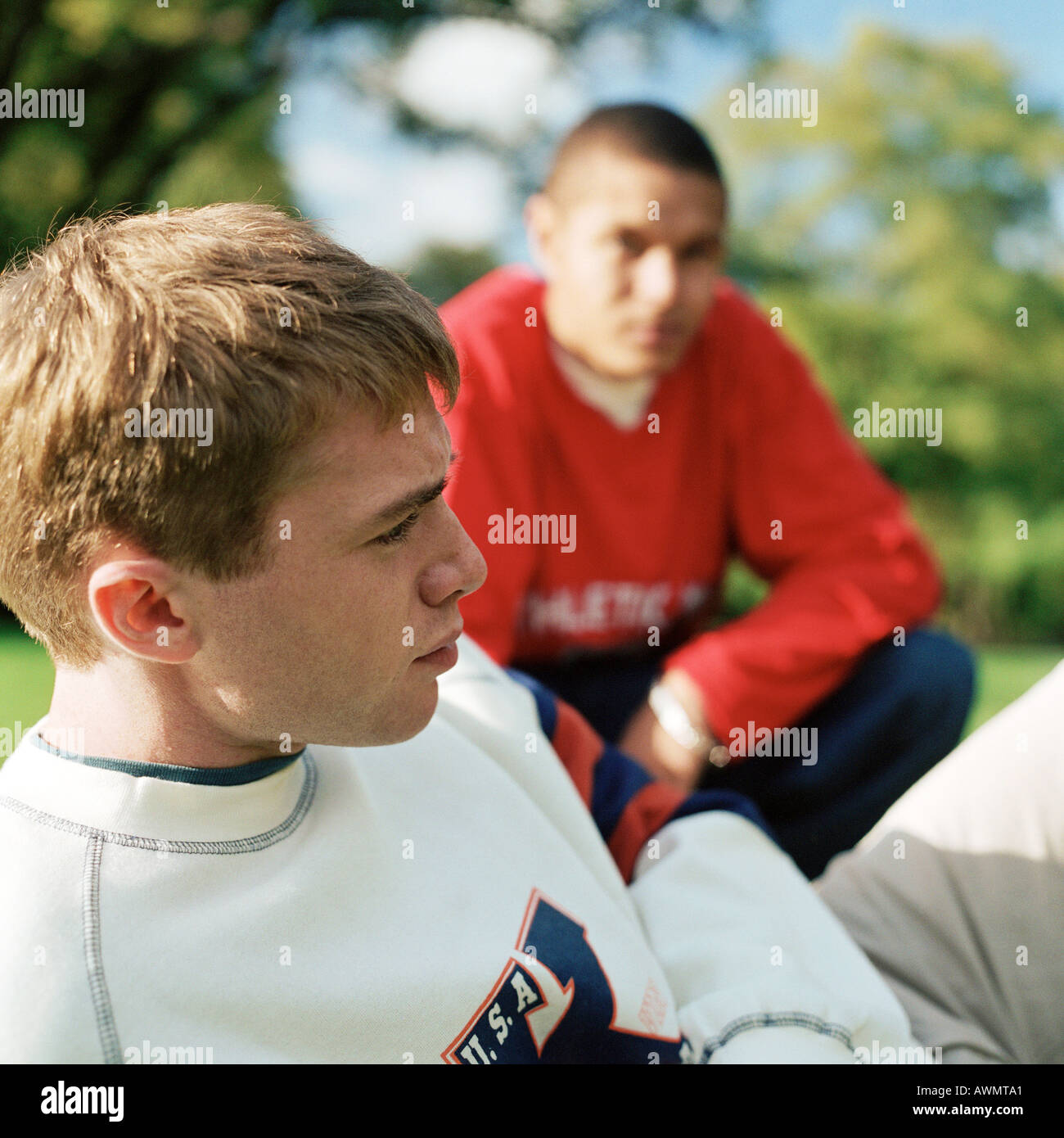 Close up of young man sitting outside, second young man crouching in ...