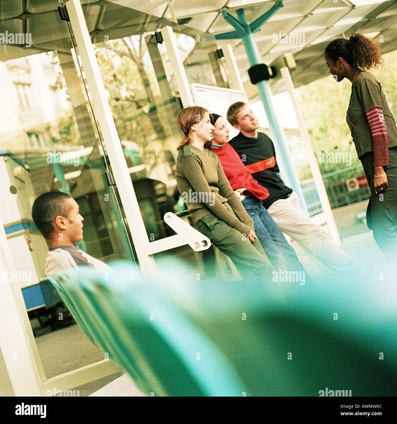 Young people talking together outside at bus station, blurred seats in ...