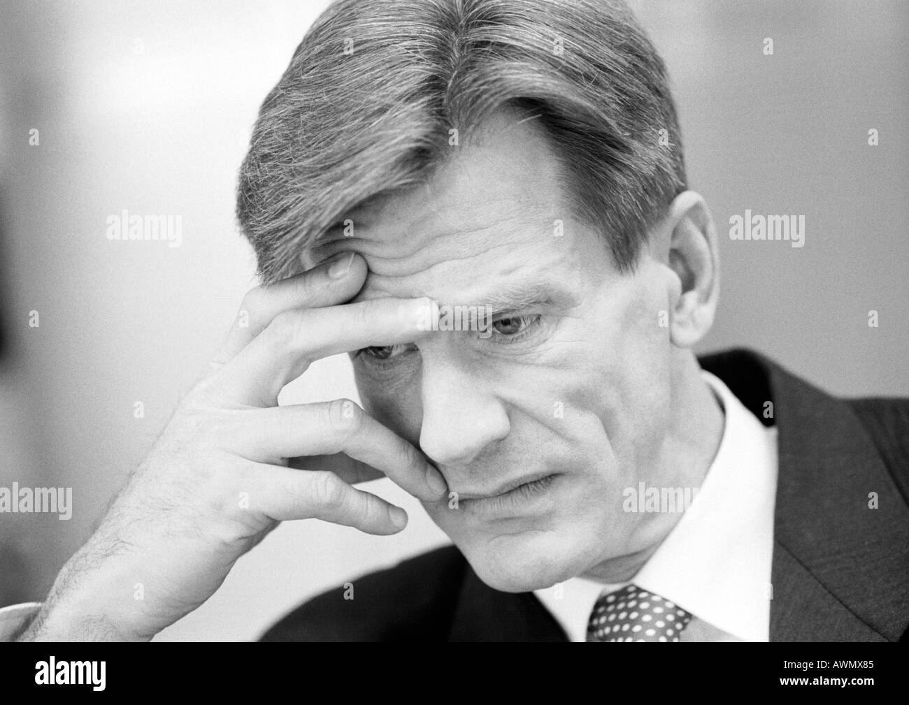 Businessman leaning head forward, holding face with fingers, close-up ...