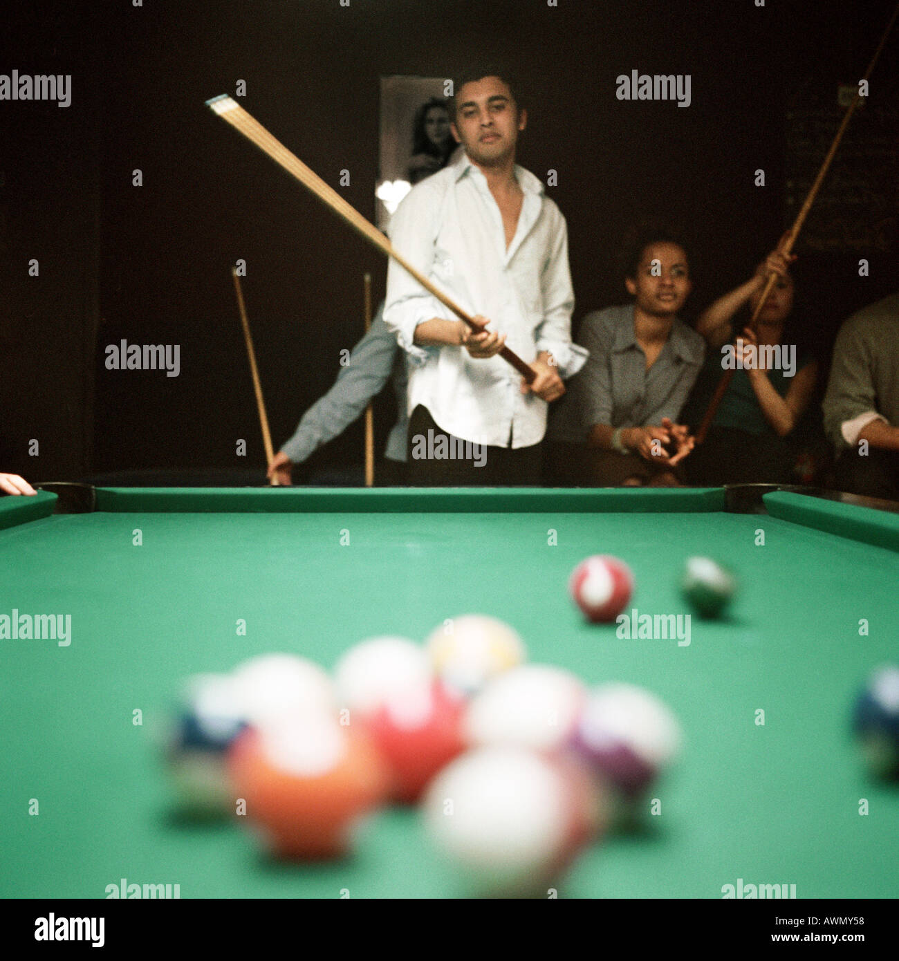 Young man shooting pool, people watching in background, billiard balls ...