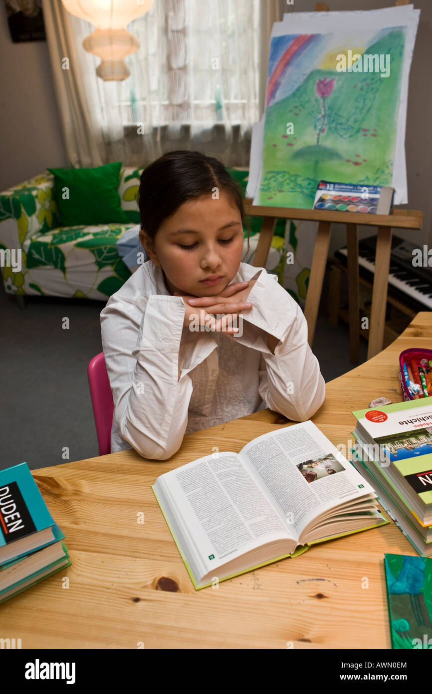 Young schoolgirl doing homework in nursery, reading book and ...